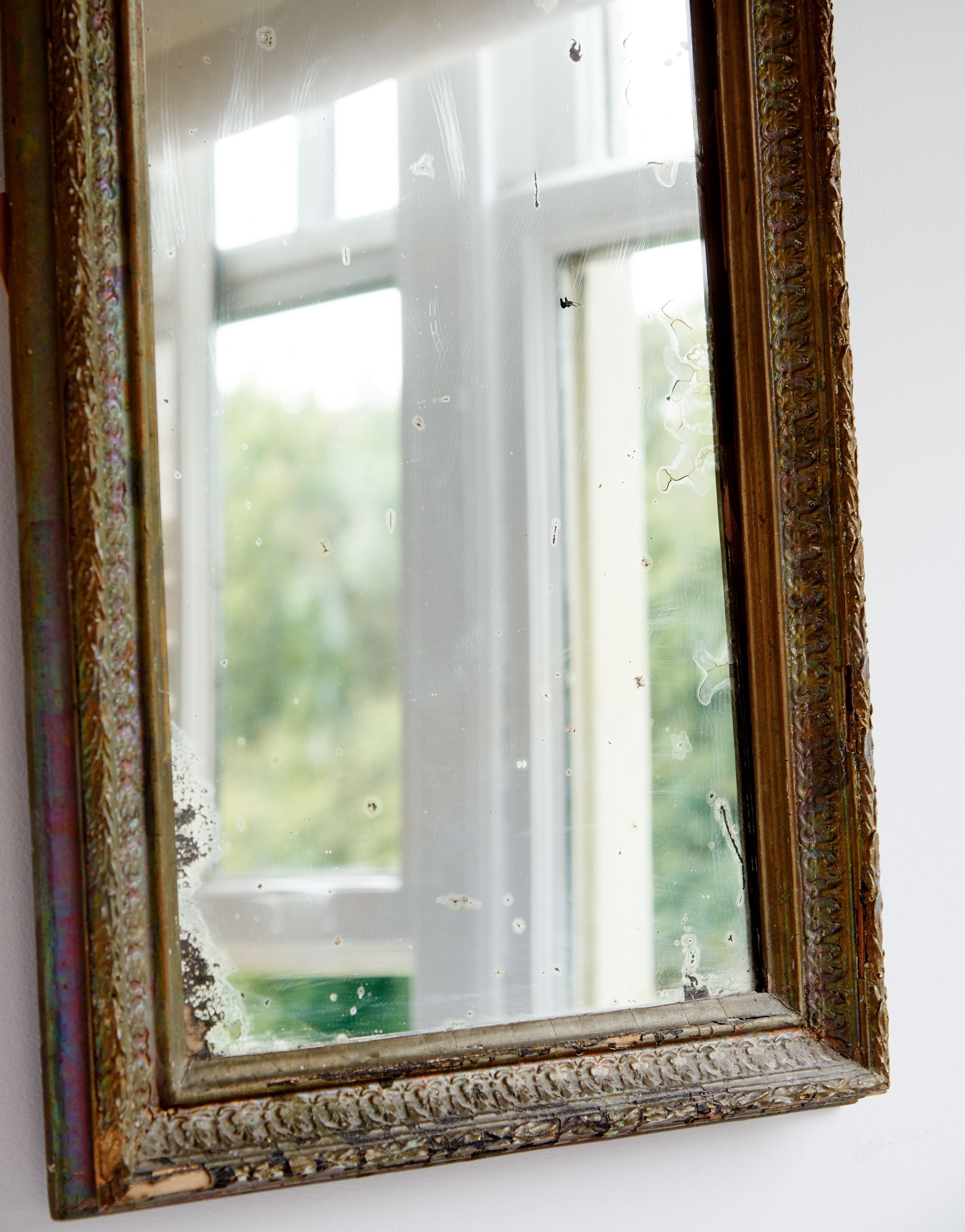 Espelho com moldura decorativa, refletindo uma janela com vista para o verde lá fora.
