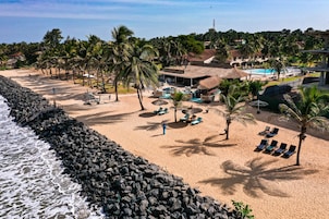 Um resort à beira-mar com piscina, palmeiras e uma linha costeira rochosa.