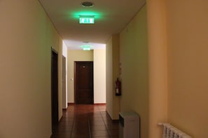 Um corredor estreito com um extintor preso na parede, uma porta no final e um sinal de saída acima da porta.
