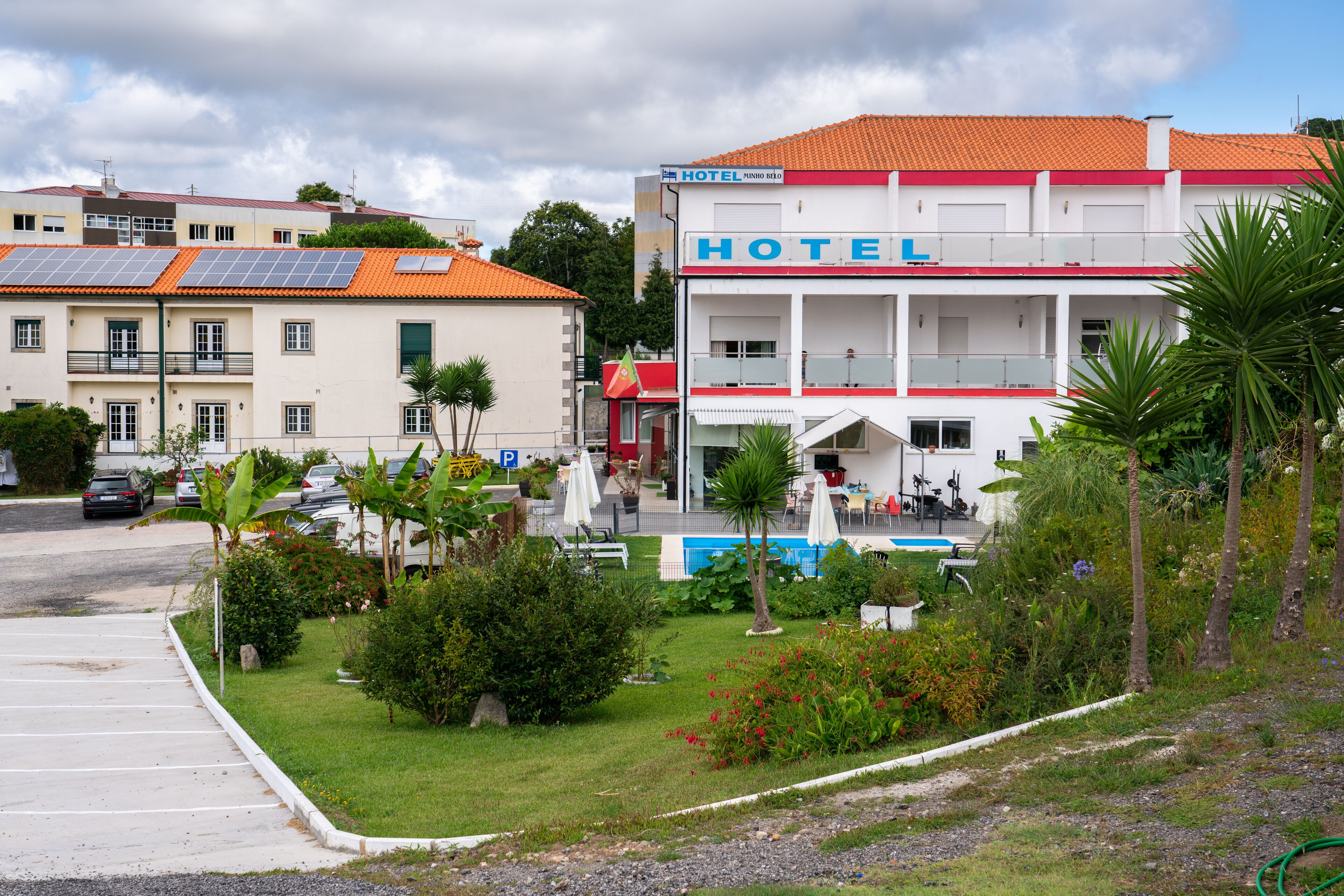 Um hotel com telhado de telhas vermelhas, piscina e vegetação exuberante.