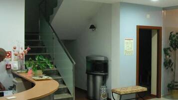 Uma área de recepção com balcão, escada, lixeira e um banco.