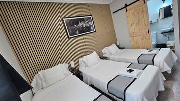 Quarto de hotel com três camas, painel de ripas de madeira, quadro emoldurado e porta deslizante de madeira.