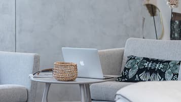 Quarto moderno com um sofá cinzento, uma pequena mesa redonda com um laptop e uma cesta de vime.