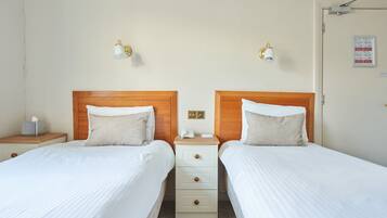 Quarto de hotel com duas camas, uma mesa de cabeceira com abajur e uma porta com placa.