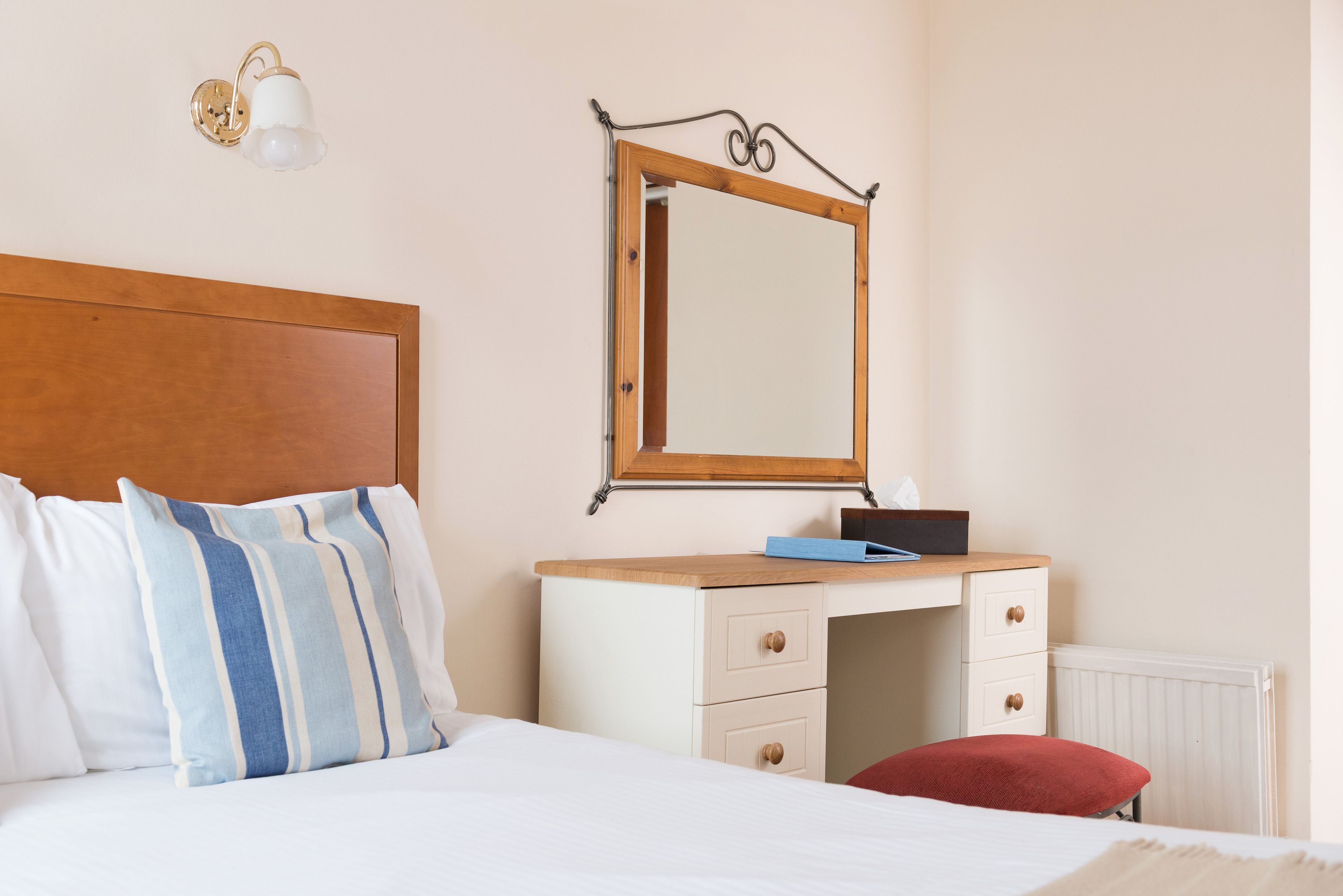 Quarto com cabeceira de madeira, mesa de cabeceira com gavetas, espelho e luminária na parede.