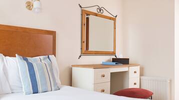 Quarto com cabeceira de madeira, mesa de cabeceira com gavetas, espelho e luminária na parede.
