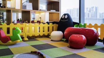Uma área de recreação infantil com um conjunto de trens, uma casinha amarela e um brinquedo de pelúcia preto grande.