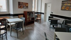 Uma área de refeições com mesas, cadeiras, uma estante de livros e um quadro na parede.