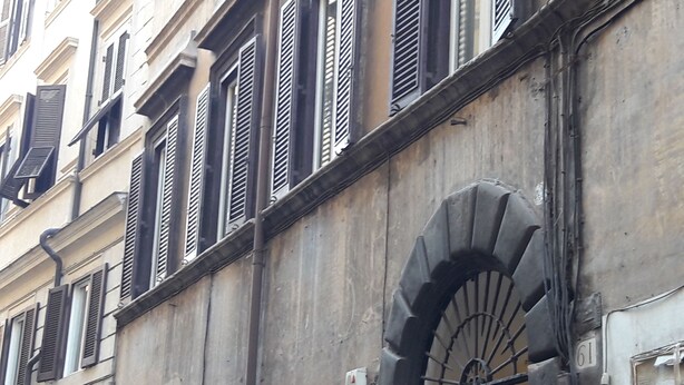 Fachada de edifício com várias janelas, algumas com persianas, e uma grande entrada em arco.