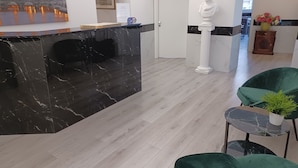 Uma área de recepção com balcão de mármore, busto de escultura, quadro emoldurado e uma porta com a inscrição '3'.