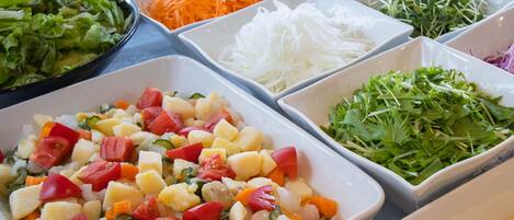 Diversas verduras frescas e saladas em recipientes brancos, dispostas sobre uma mesa.