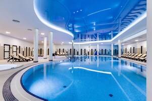 Piscina interior com água azul cristalina, rodeada por espreguiçadeiras e um design moderno no teto.