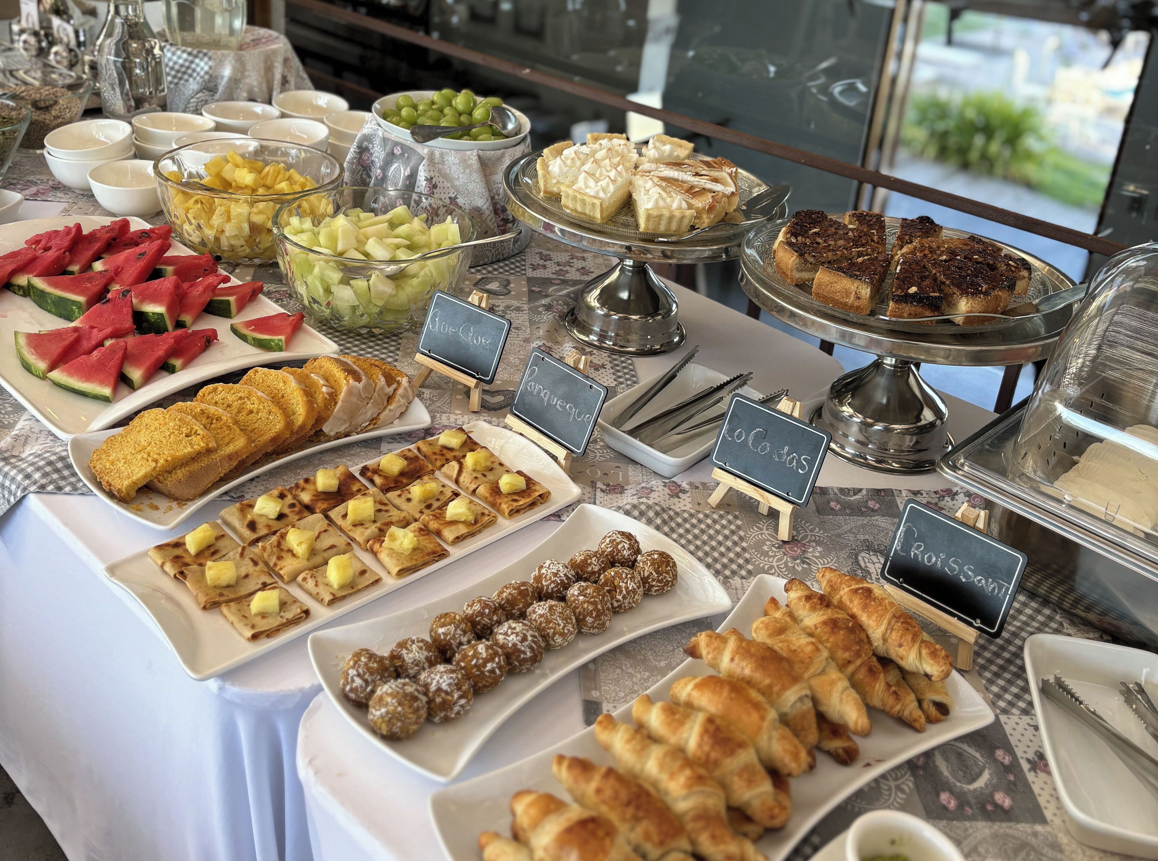 Buffet com diversas opções de comida, incluindo frutas, doces e sobremesas.