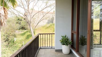 Uma varanda com vista para uma área gramada e árvores, um vaso de planta e uma janela com vista para a paisagem.