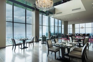 Ampla sala de jantar com grandes janelas que oferecem vista da cidade, luminárias elegantes e móveis modernos.