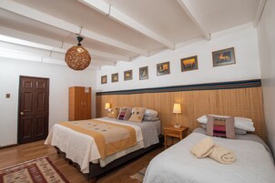 Quarto de hotel com uma cama grande, uma cama menor, um guarda-roupa, uma luminária pendente e uma parede com quadros.