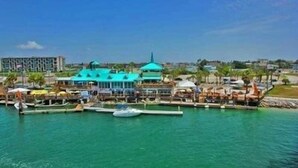 Um hotel na orla marítima com um edifício azul-turquesa, barcos atracados e um céu azul límpido.