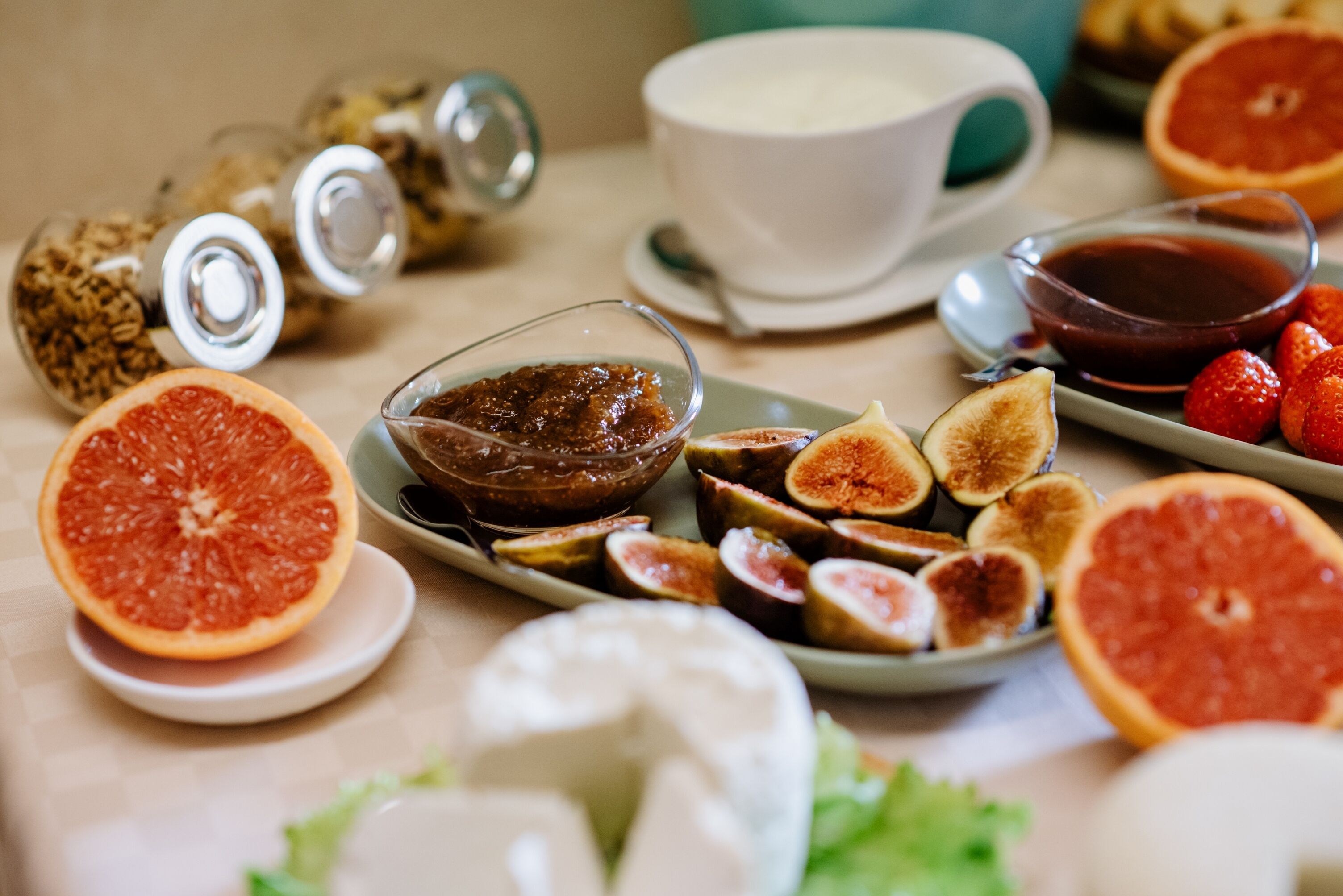 Uma mesa de café da manhã com metades de toranja, figos, morangos e uma tigela de geleia.