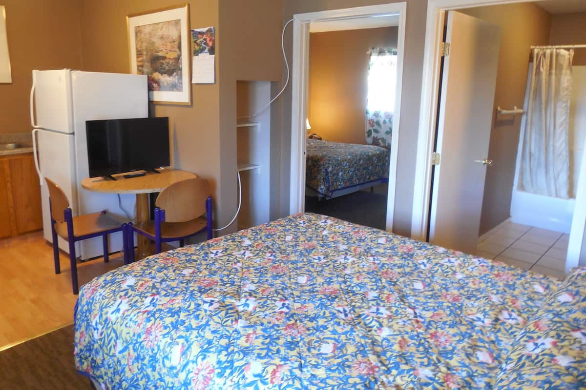 Quarto com cama, escrivaninha com cadeira, televisão e porta para um banheiro.