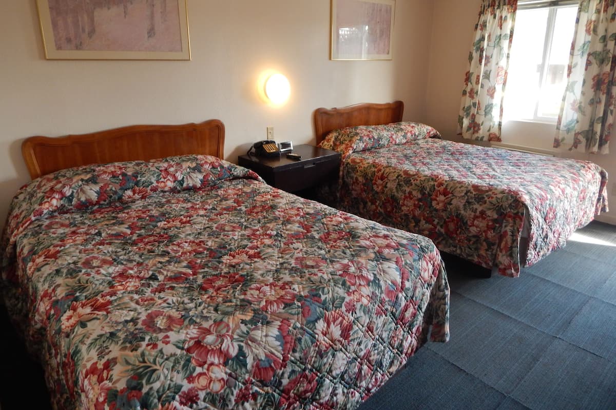 Quarto de hotel com duas camas, cada uma com roupa de cama floral, uma mesa de cabeceira com abajur e uma janela com cortinas florais.
