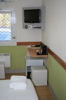 Quarto de hotel com uma cama, uma televisão na parede, uma secretária pequena com uma cafeteira e uma janela com vista.