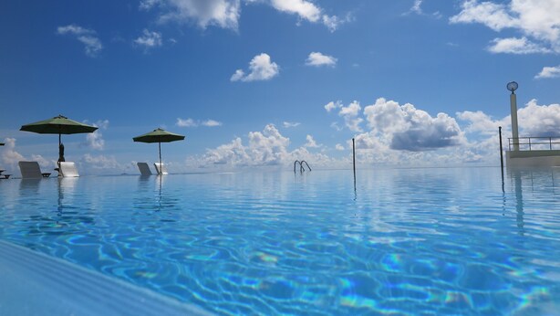 Piscina azul límpida com espreguiçadeiras e guarda-sóis, sob um céu claro e com nuvens.