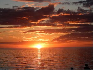 Pôr do sol sobre o oceano com silhuetas de pessoas em primeiro plano.
