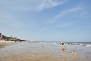 Uma praia com areal dourado, algumas pessoas e céu limpo.