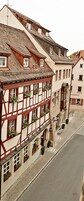 Um edifício tradicional em enxaimel com várias janelas, algumas adornadas com caixas de flores, e uma rua à frente.