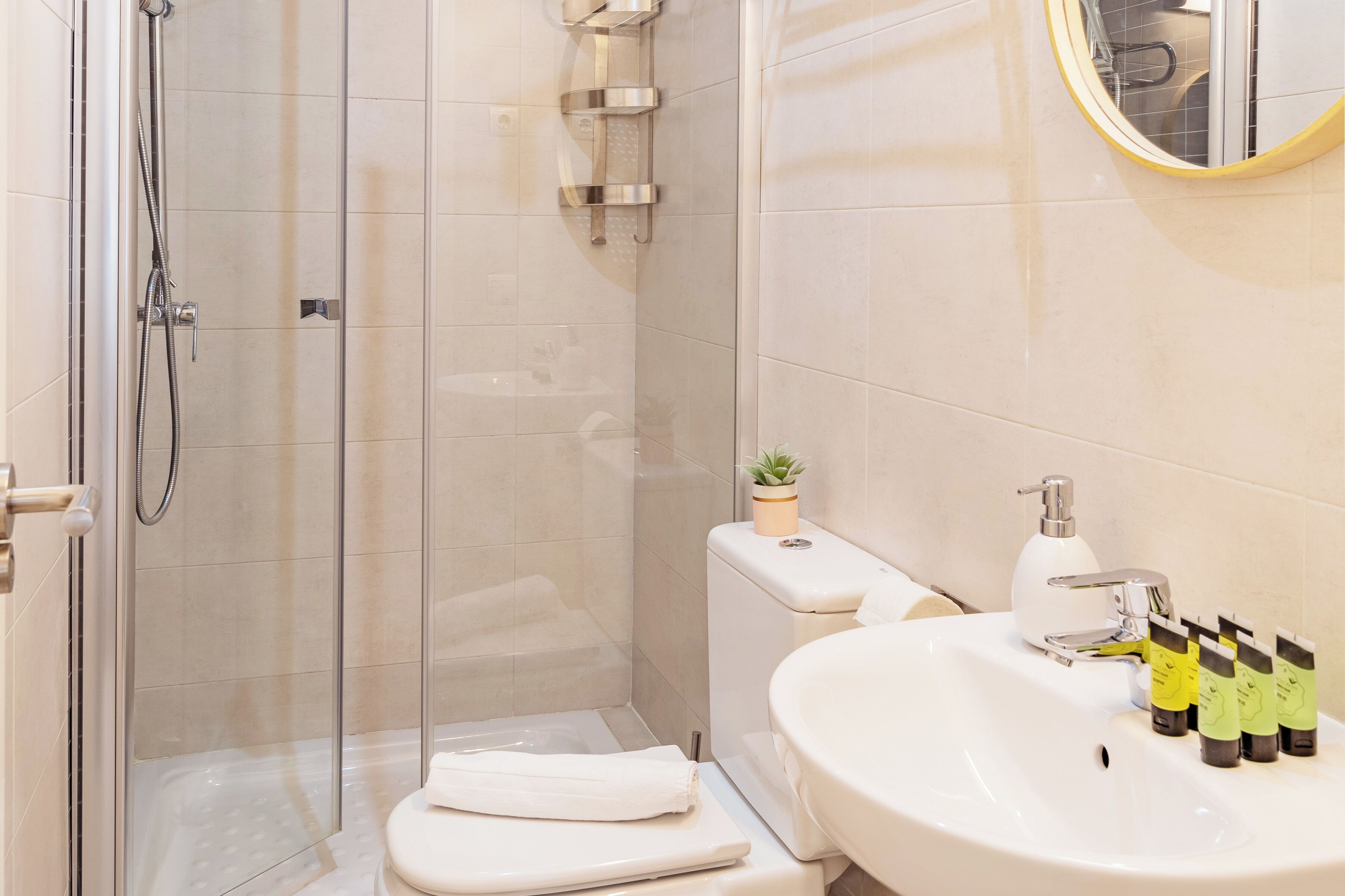 Casa de banho moderna com chuveiro em cabine de vidro, sanita branca e lavatório com produtos de higiene pessoal.