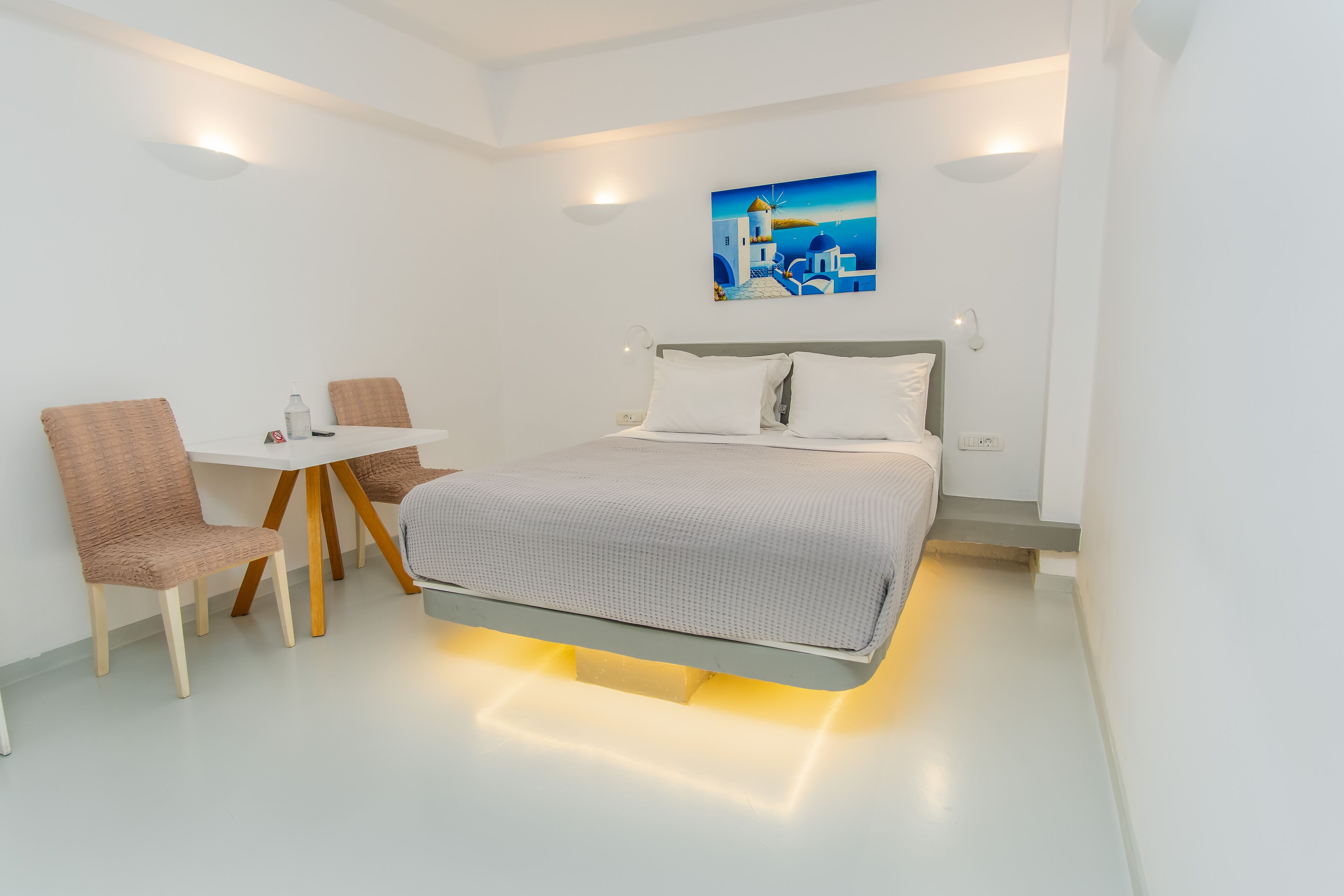 Quarto de hotel moderno com uma cama, uma mesinha, duas cadeiras e um quadro na parede.