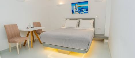 Quarto de hotel moderno com uma cama, uma mesinha, duas cadeiras e um quadro na parede.