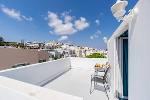 Terraço no telhado com mesa e cadeiras, com vista para uma cidade costeira com edifícios brancos e um céu azul claro.