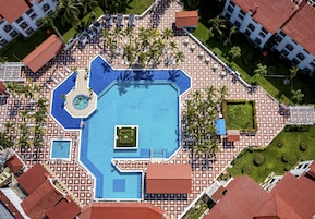 Vista aérea de um resort com uma piscina central, várias áreas de descanso e palmeiras.