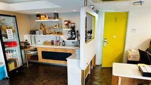 Uma cozinha com geladeira, prateleiras com alimentos, máquina de café e uma porta amarela.