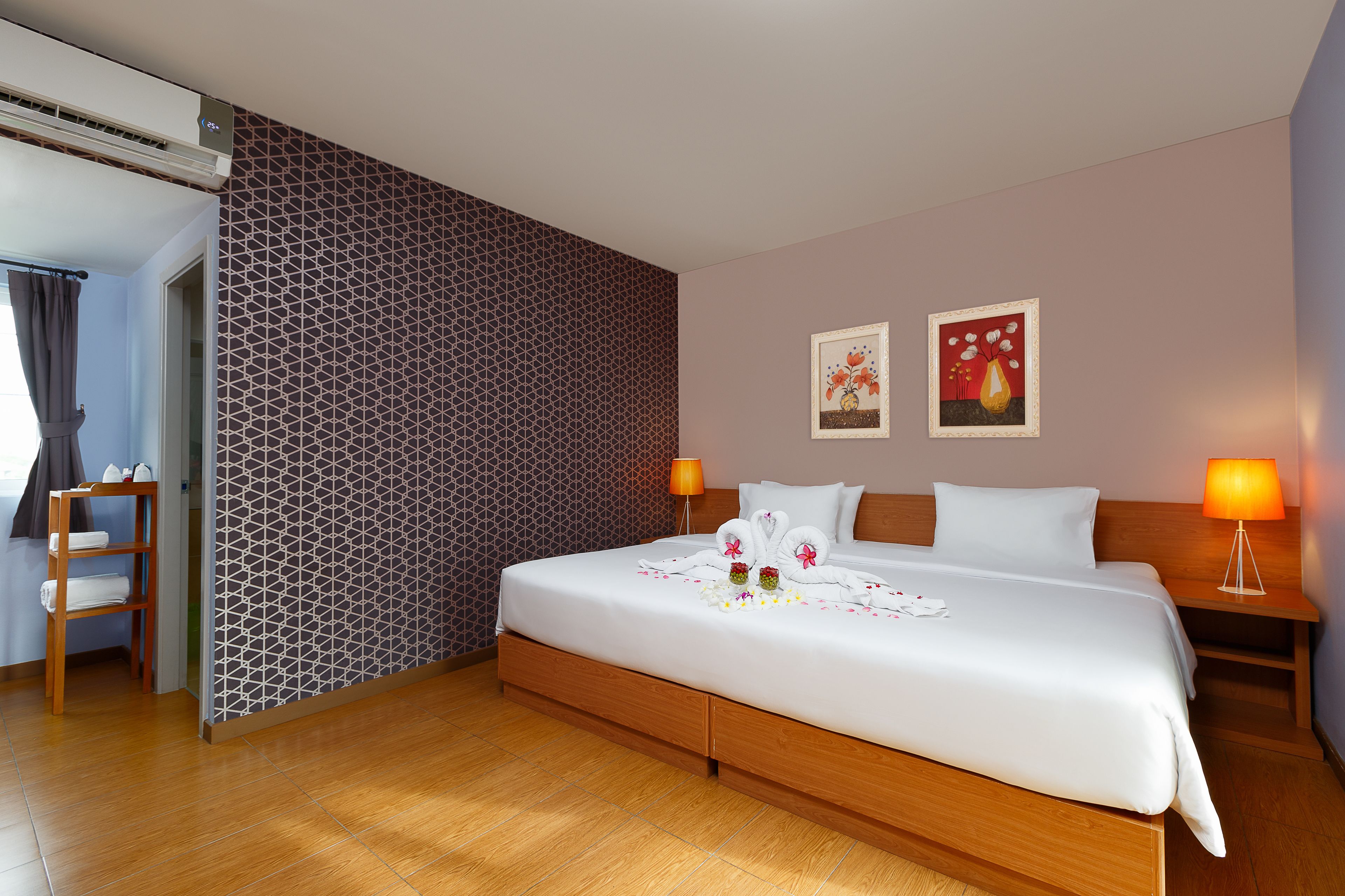 Quarto de hotel com uma cama grande, duas luminárias de cabeceira, uma mesinha de cabeceira de madeira, uma parede com padrão geométrico e um pequeno armário com toalhas.