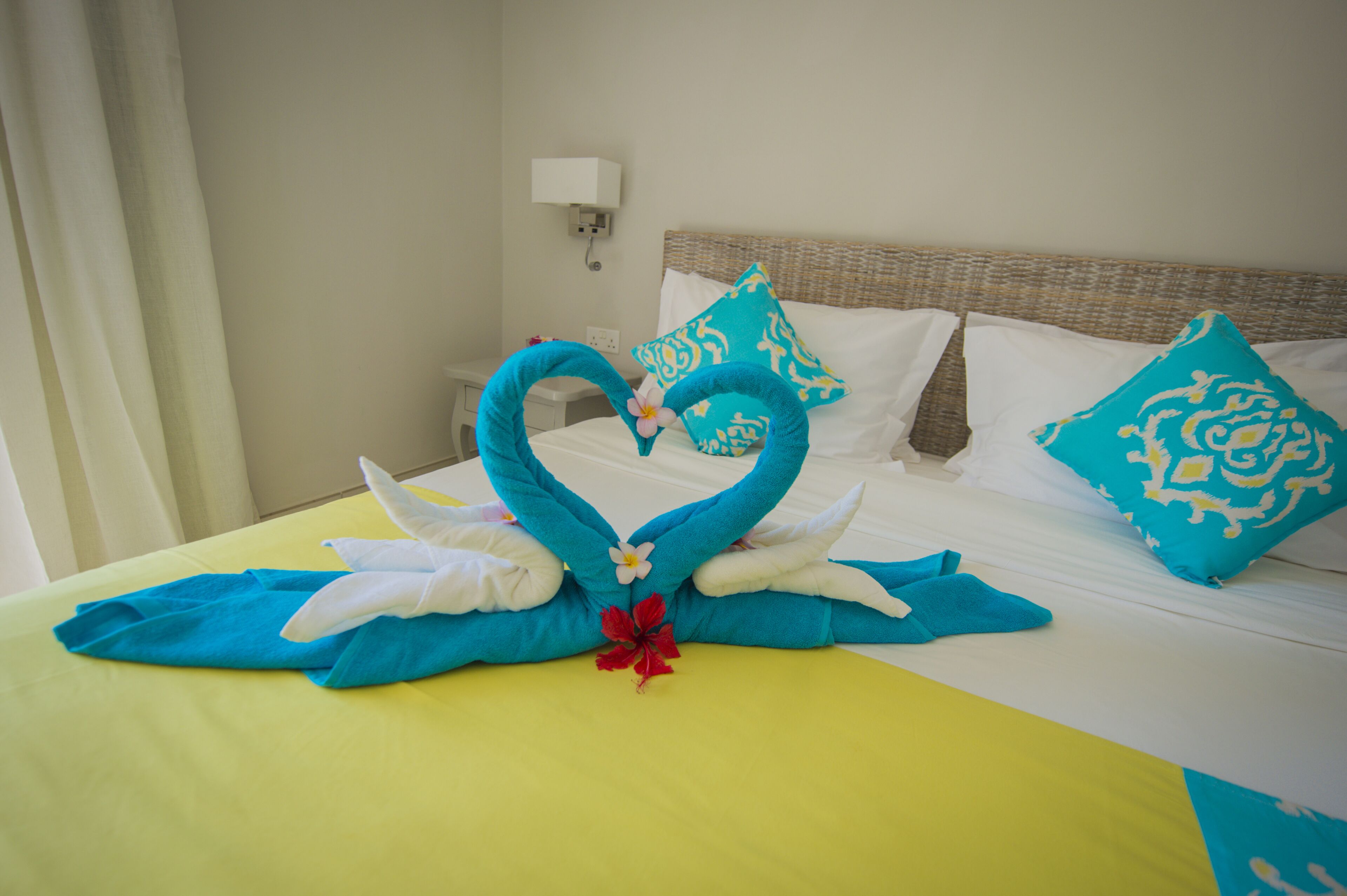 Cama com arranjo de toalha azul em formato de coração, travesseiro branco e travesseiro azul estampado.