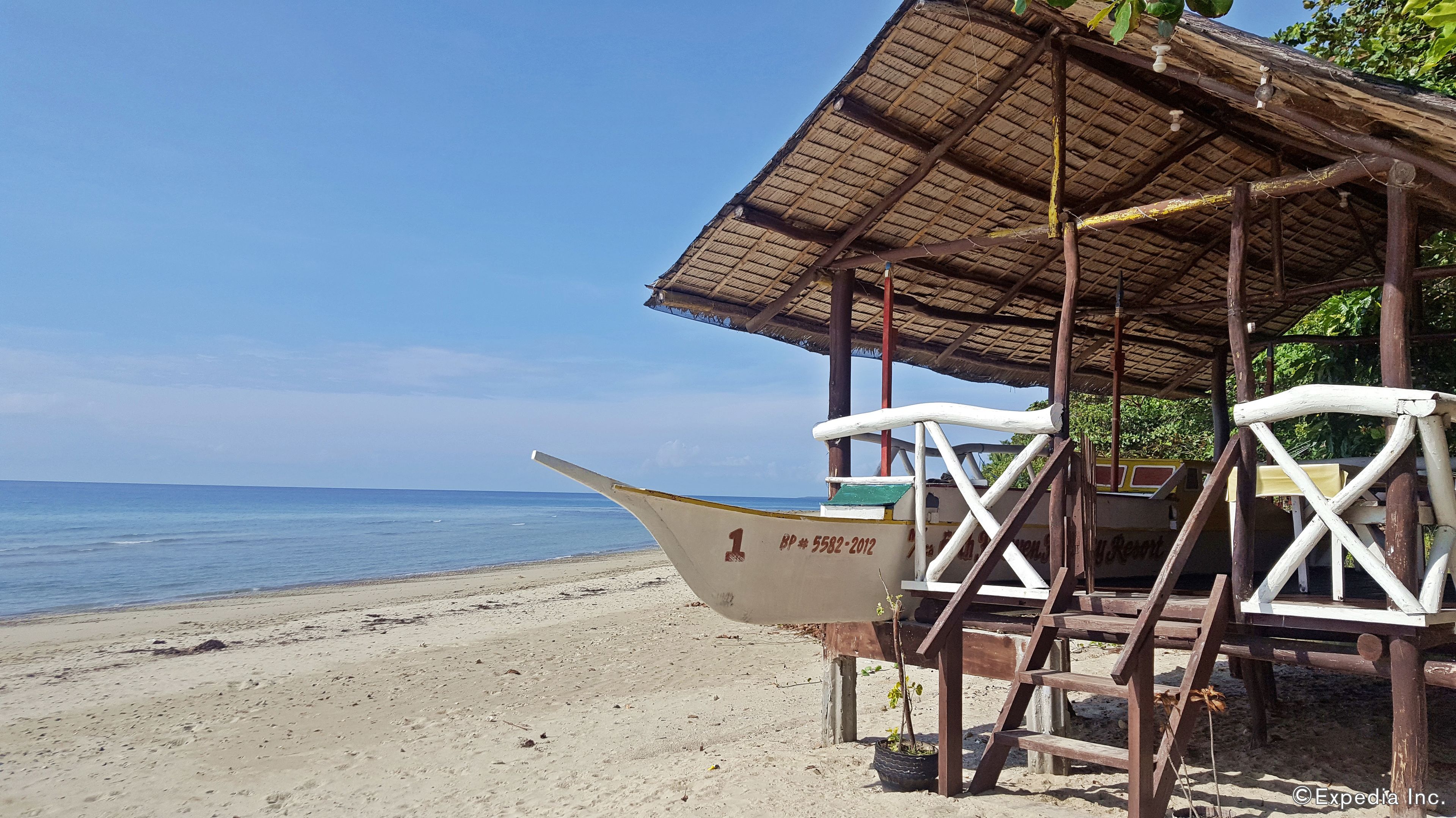 Uma cabana de praia com um barco identificado com o número '1' e 'BP# 5582-2012' numa praia de areia.