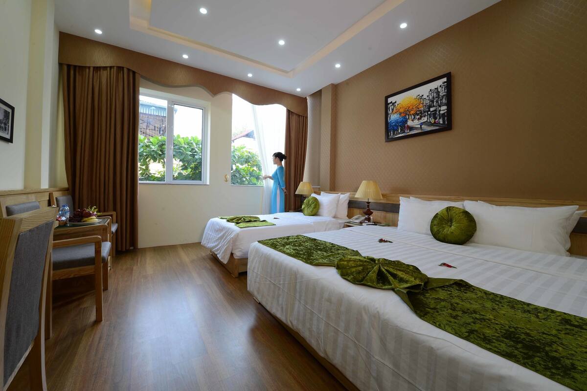 Quarto de hotel com duas camas, uma escrivaninha e uma janela com cortinas.