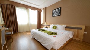 Quarto de hotel com cama de madeira, uma escrivaninha com abajur e um quadro na parede.