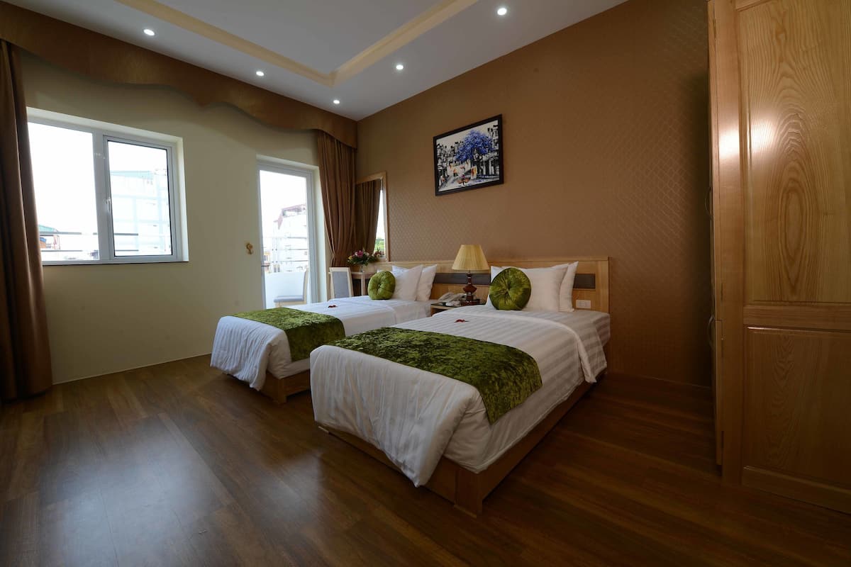 Quarto de hotel com duas camas, soalho de madeira, uma janela grande e um quadro na parede.