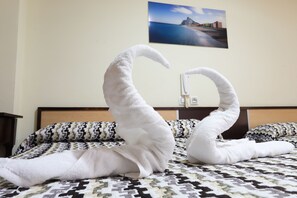 Uma cama com colcha estampada e duas toalhas dispostas em formato de coração.
