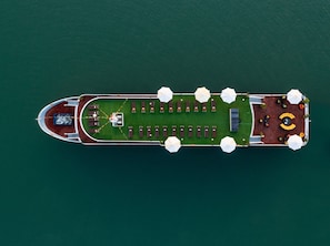 Vista aérea de um navio de cruzeiro com área de convés, que inclui fileiras de espreguiçadeiras, guarda-sóis e um espaço de estar central.