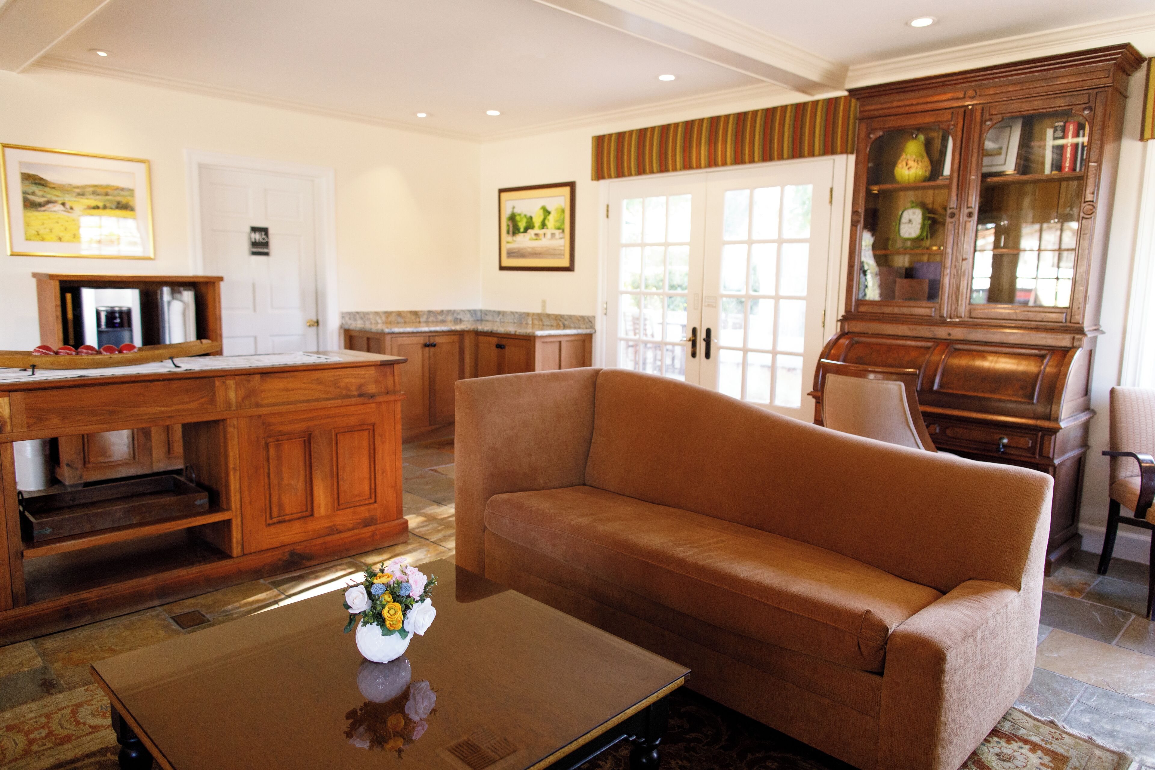 Uma sala de estar ampla com um sofá marrom, uma mesa de centro de madeira e uma área de cozinha com armários de madeira e forno embutido.