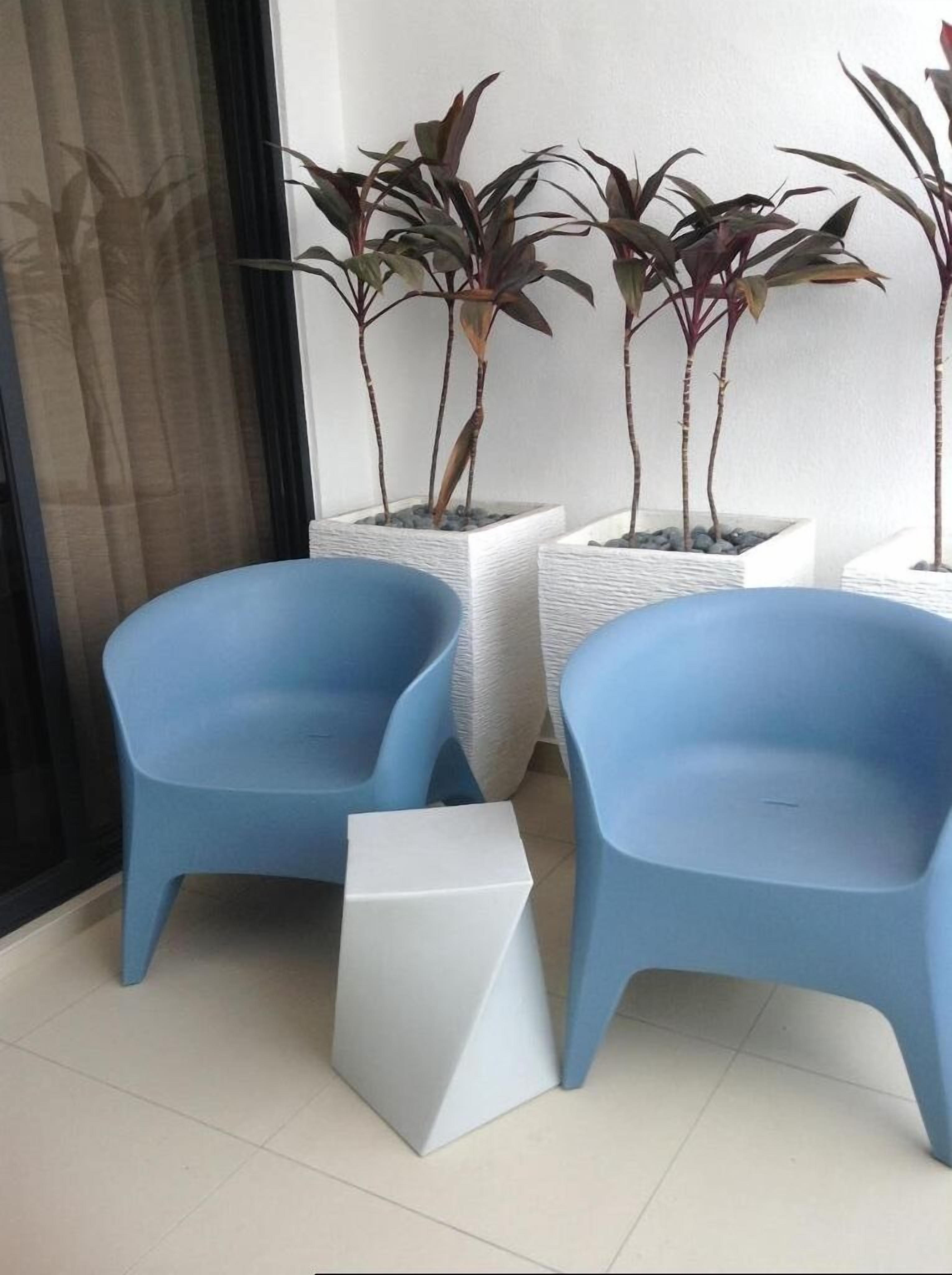 Um quarto com uma cadeira azul, uma mesa branca e uma planta.