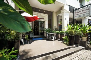 Entrada de hotel com um guarda-chuva vermelho, plantas em vasos e uma placa com o nome 'Saigon South Serviced Apartments 2'.