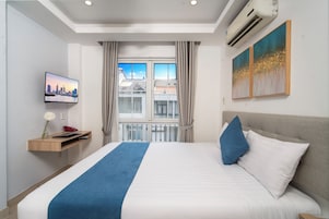 Quarto de hotel com cama, televisão, janela com cortinas e obras de arte na parede.