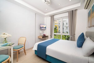 Quarto de hotel com cama, escrivaninha, cadeira, televisão e janela com vista para edifícios.