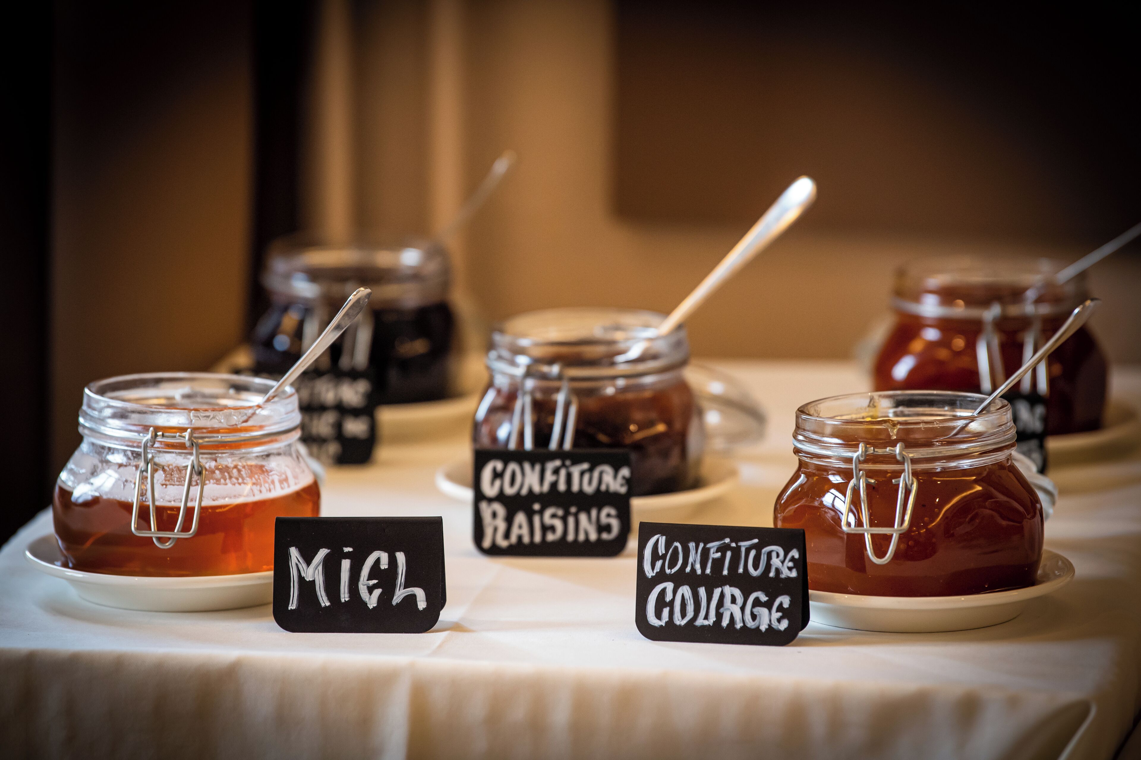 Uma mesa com potes de mel rotulados 'Miel' e 'Confiture Gorgée'.