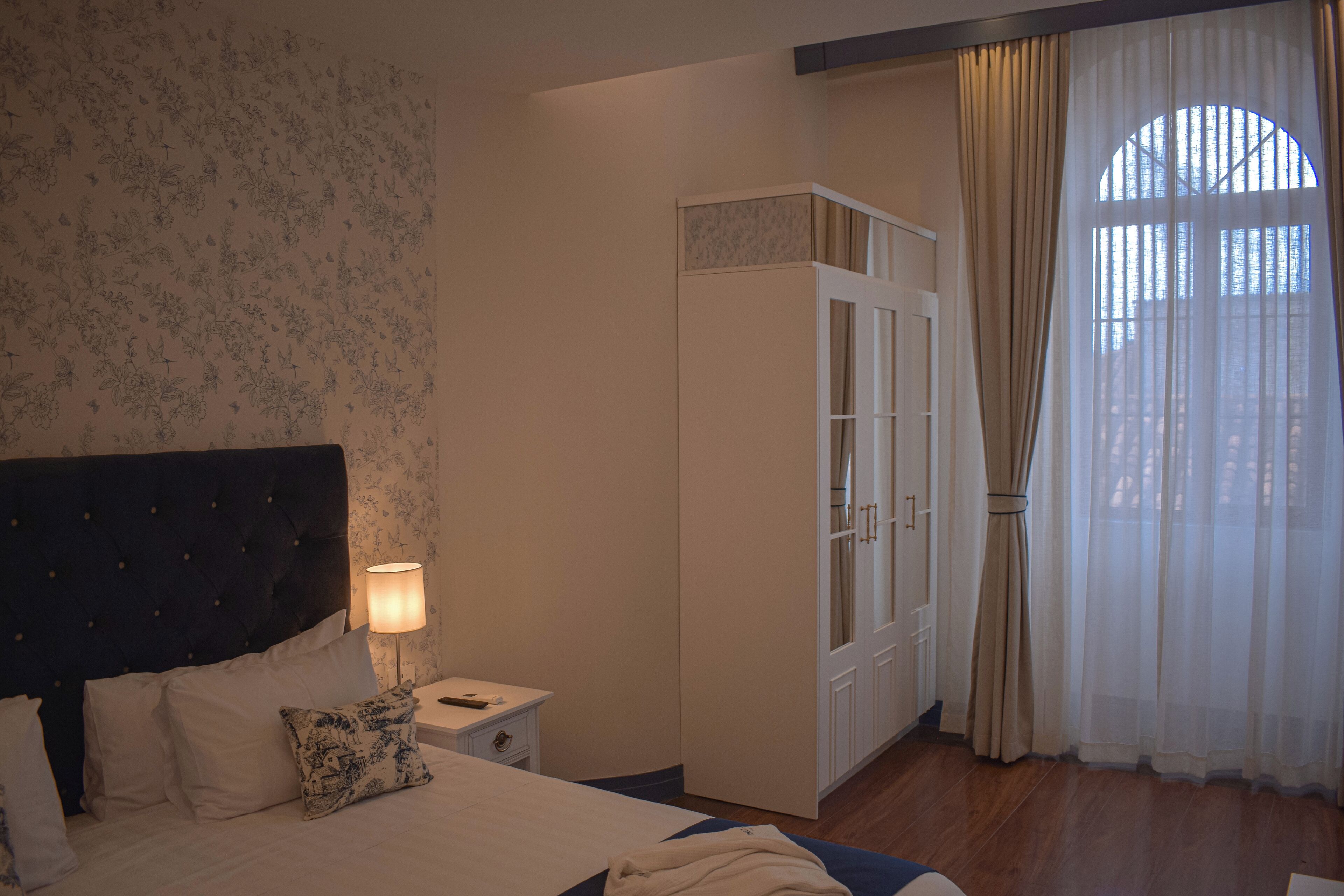 Quarto com cama, mesa de cabeceira, guarda-roupa e janela com cortinas.